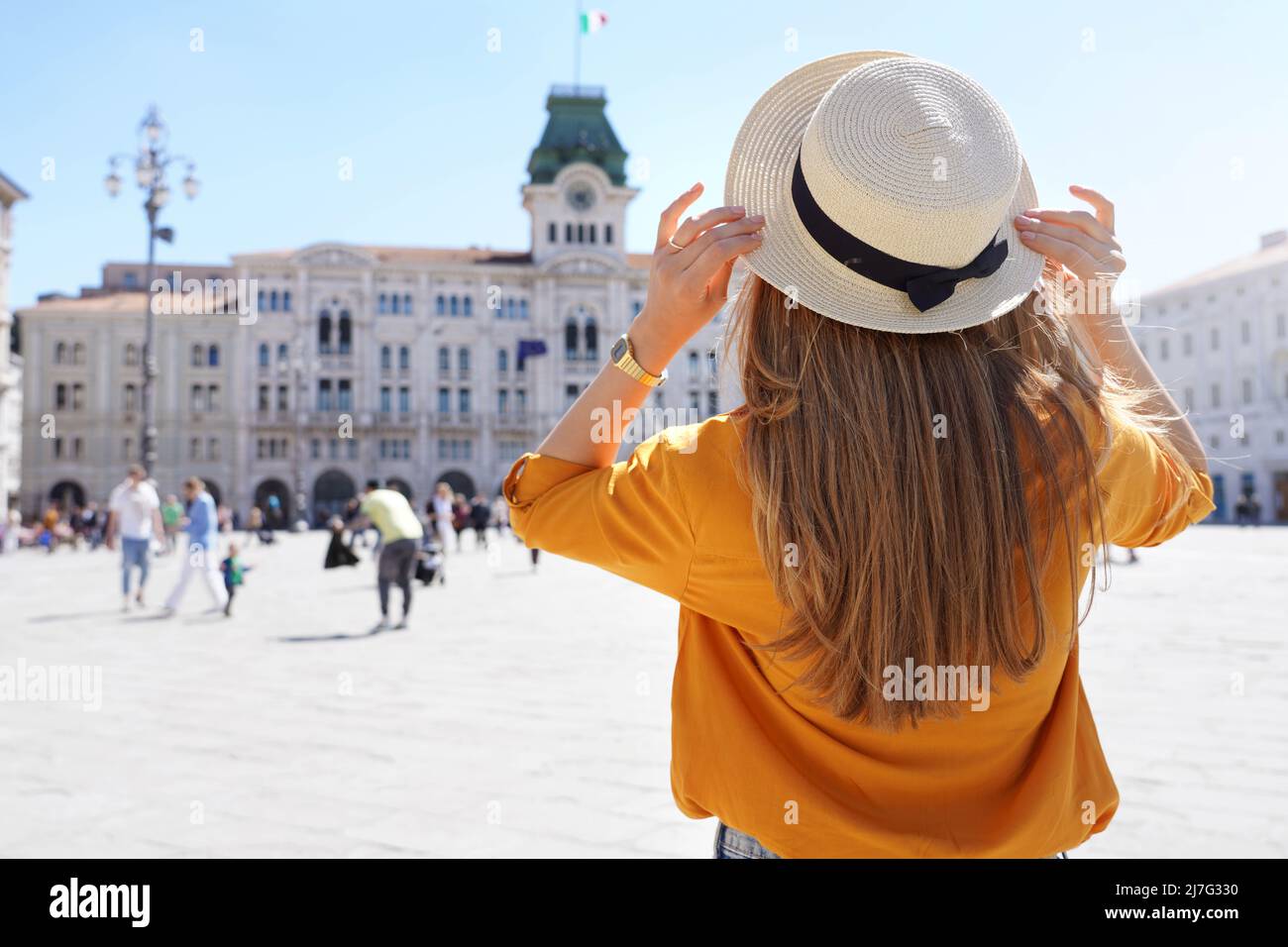 Tourism in Europe. Back view of pretty girl holding hat in Trieste ...