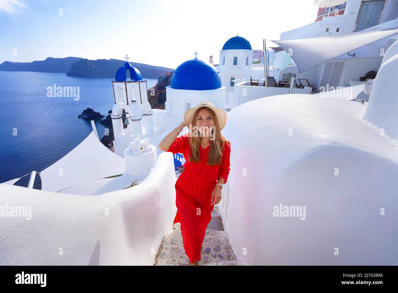 Happy traveler tourist climbs stairs in Oia, Greek traditional village with white houses and ...