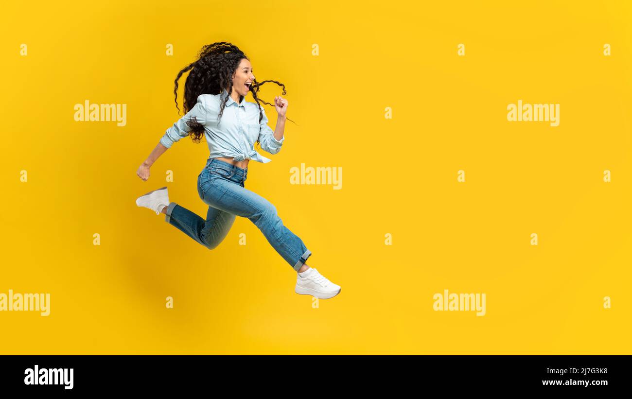 Excited young woman jumping up at orange studio Stock Photo - Alamy