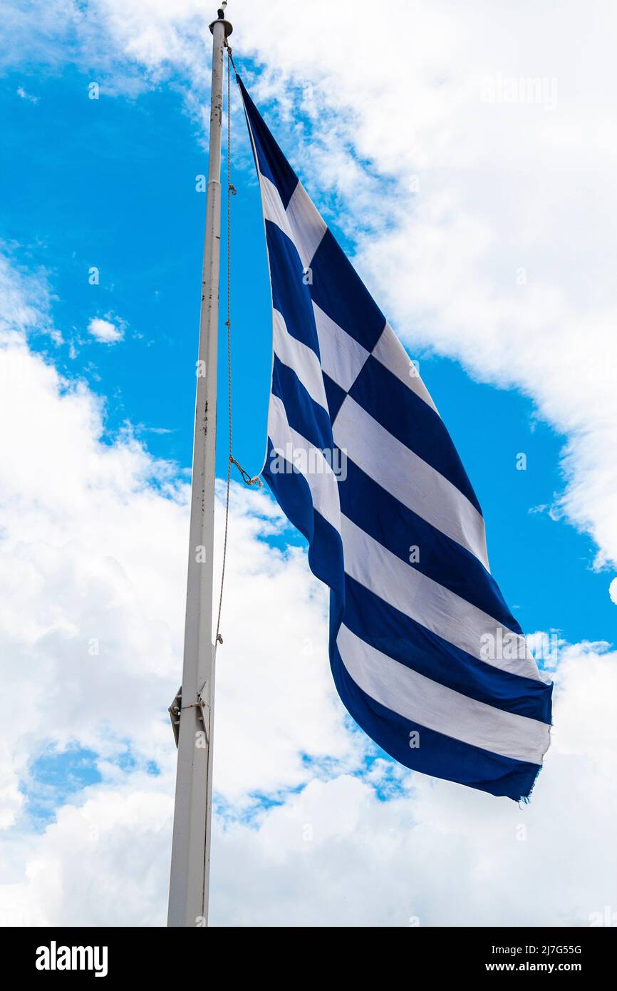 Greece flag fluttering on mast against a background of saturated blue ...