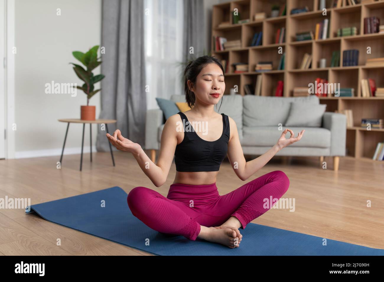 Peaceful korean lady in sportswear sitting on yoga mat with closed eyes ...
