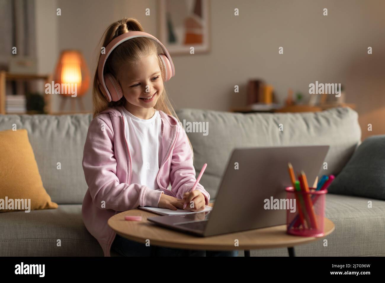 Happy Girl Using Laptop Taking Notes Wearing Earphones At Home Stock ...