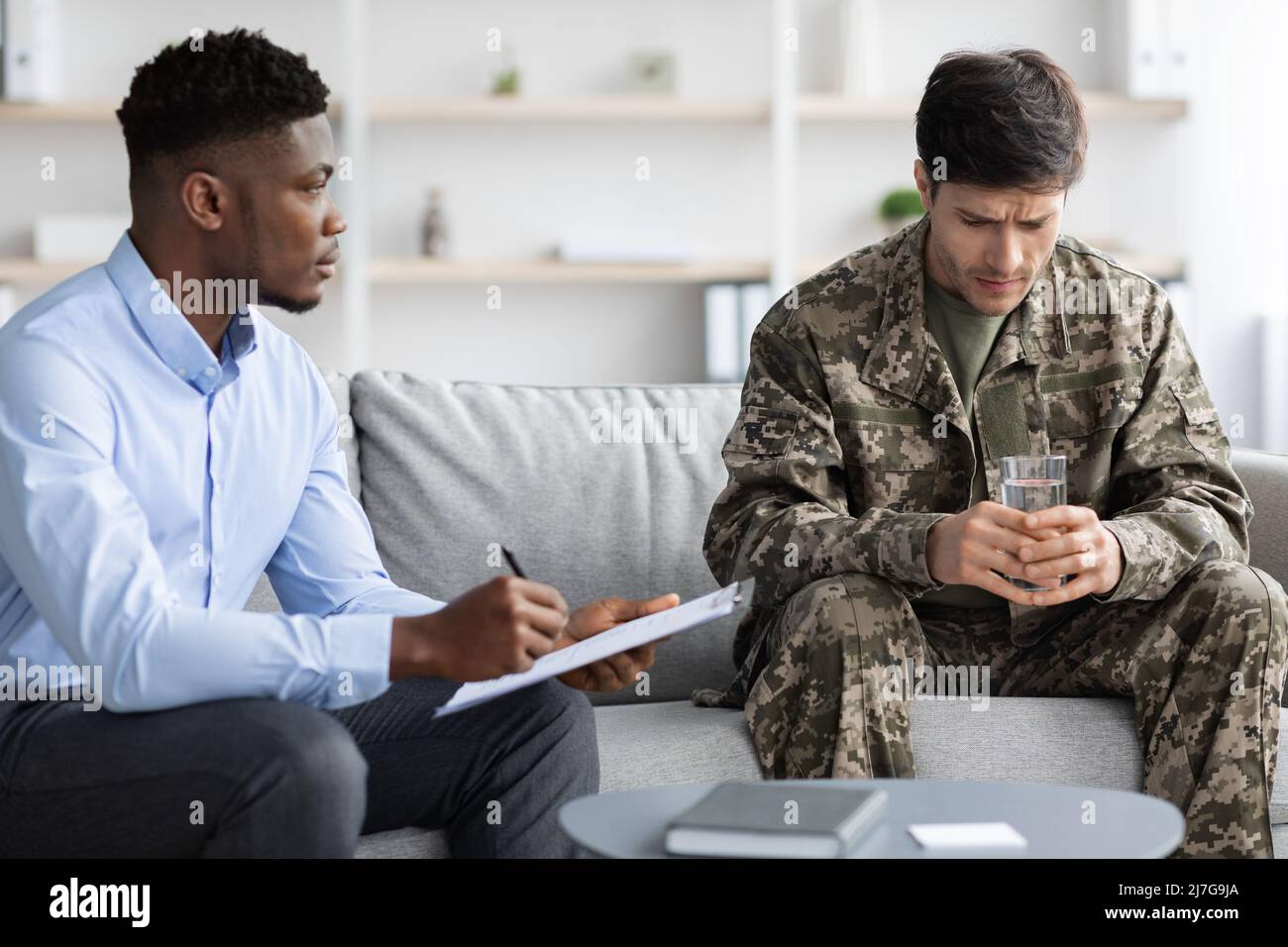 Upset soldier having therapy session with psychologist, clinic interior ...