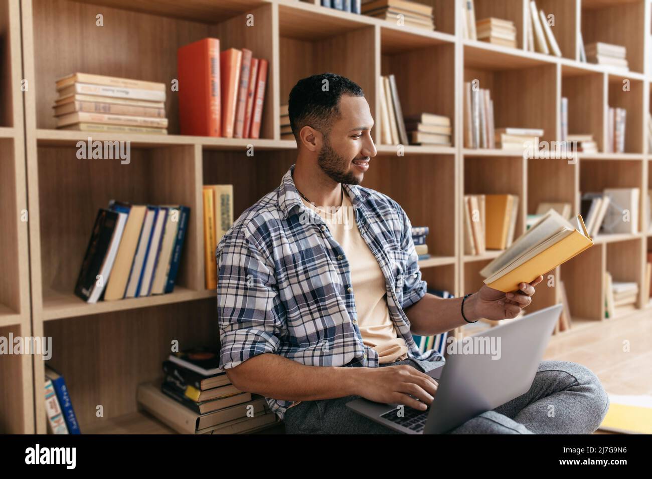 Arab man learning online, reading book and using laptop computer ...
