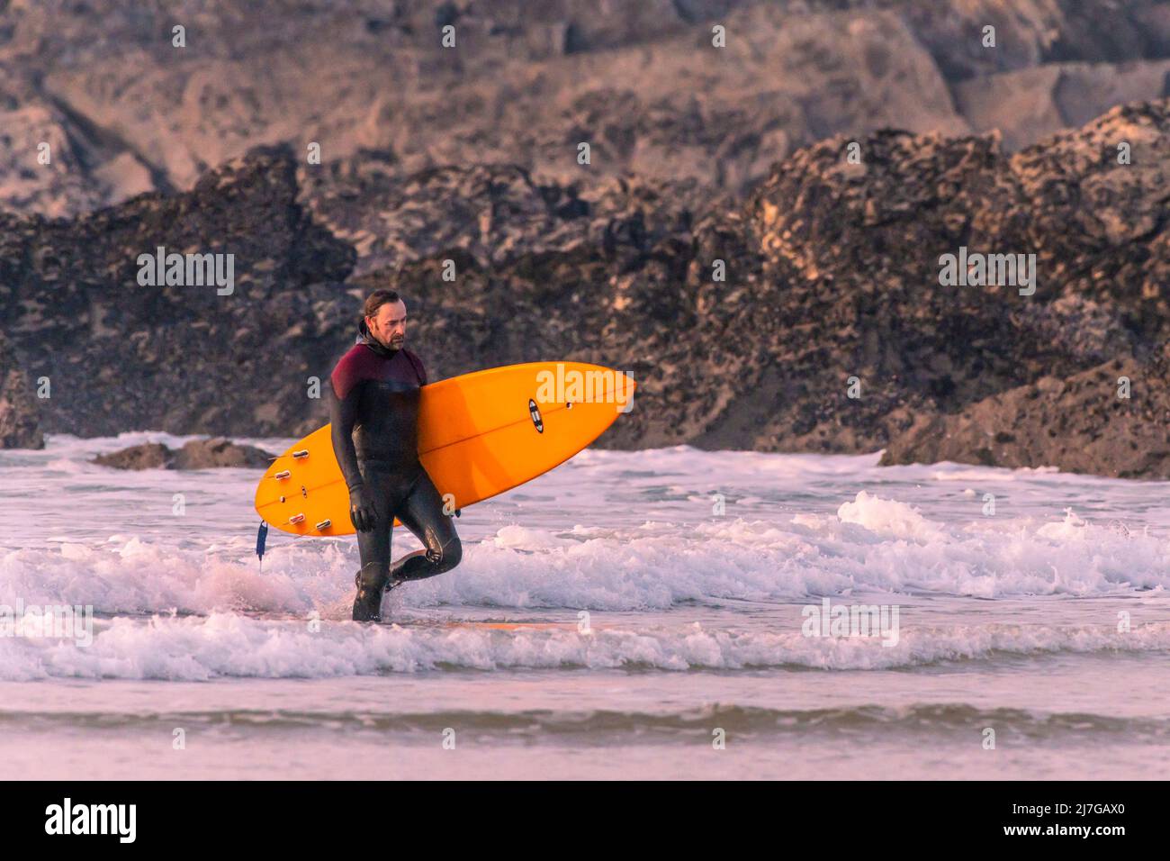 A tired surfer carrying his surfboard and walking out of the sea at ...