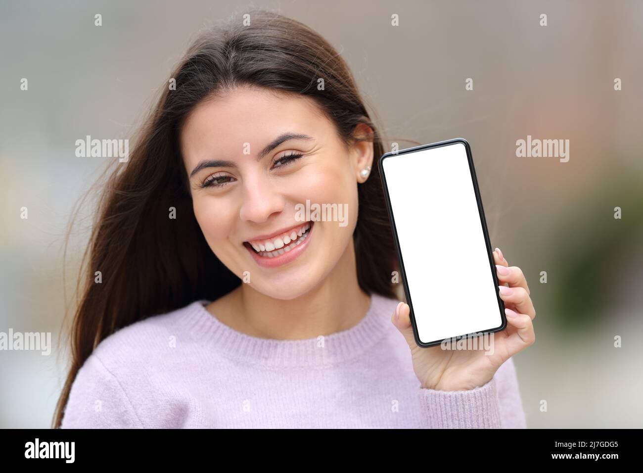 Front view portrait of a happy teen showing blank phone screen outdoors ...