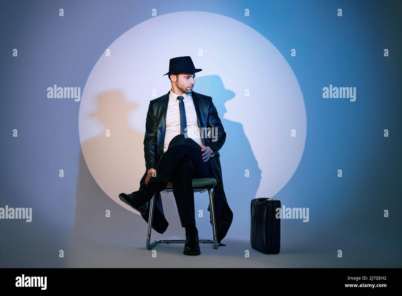Handsome private detective sitting on chair in the spotlight on studio ...