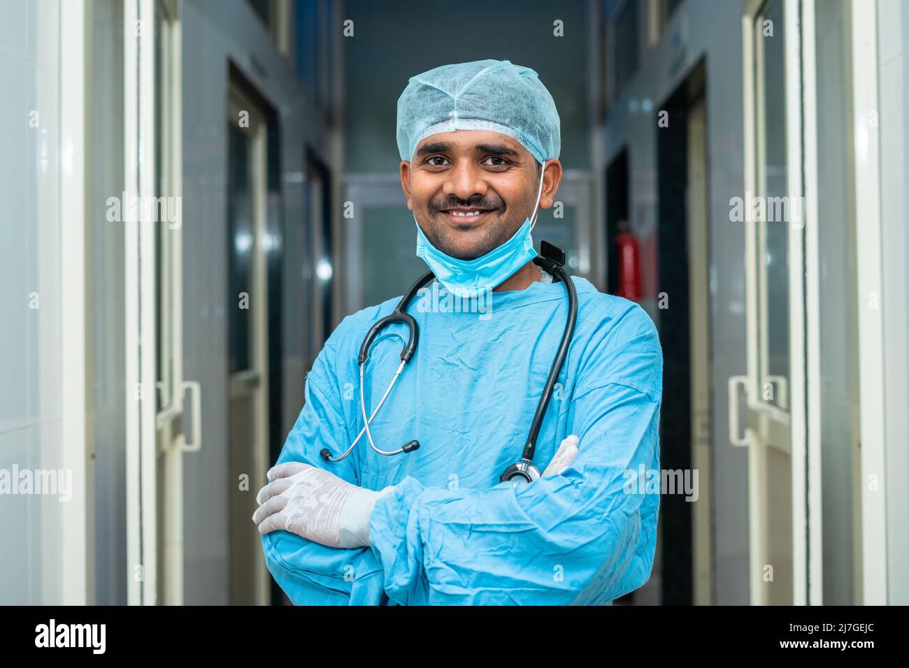 Smiling surgeon standing with crossed arms by holding stethoscope while ...