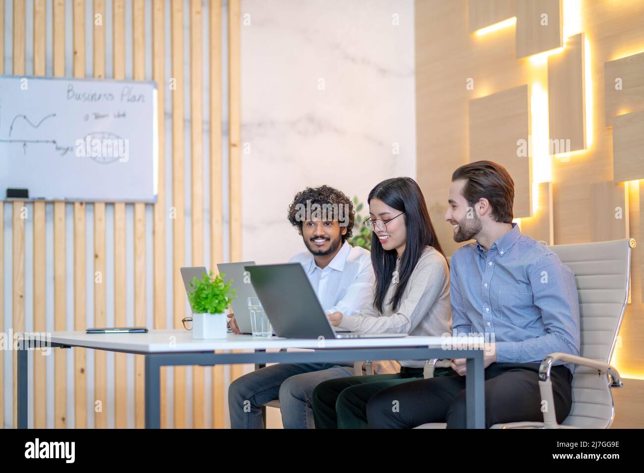 Three cheerful employees seated at the office table Stock Photo - Alamy