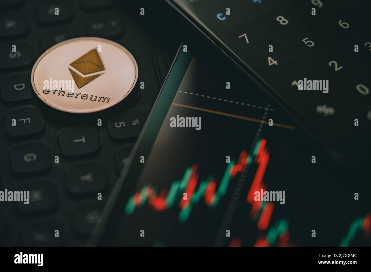 Close up of an Ethereum cryptocurrency coin near a monitor with candle ...