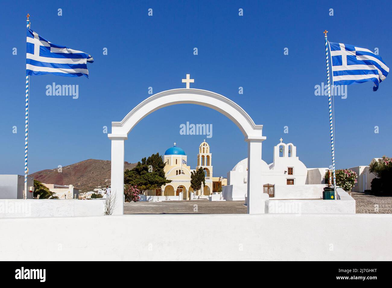 Square in the Greek village. Arch with cross, church and flags of ...