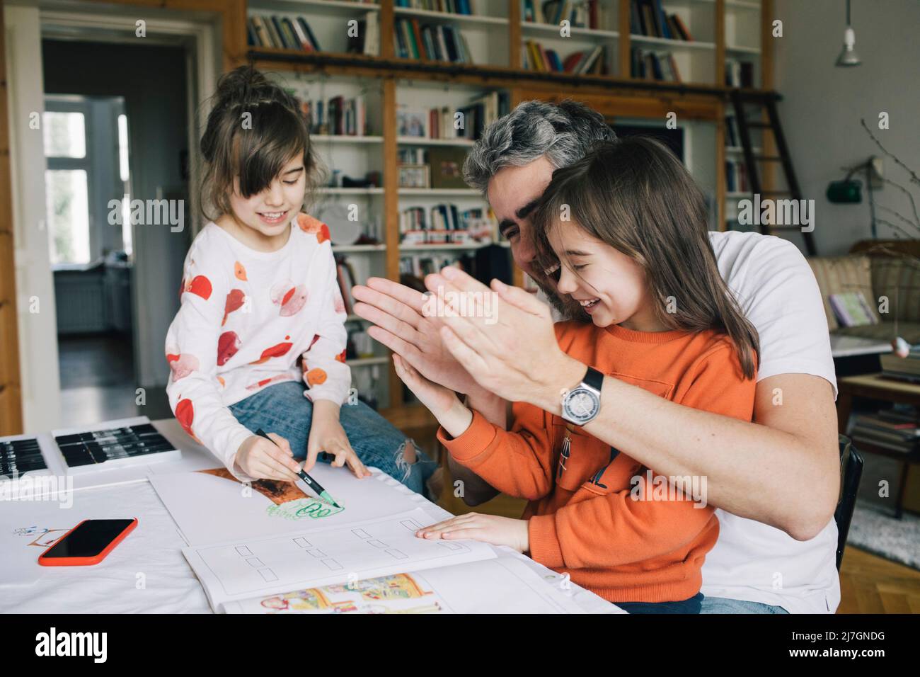 Happy father gesturing while helping daughter in doing homework by girl ...