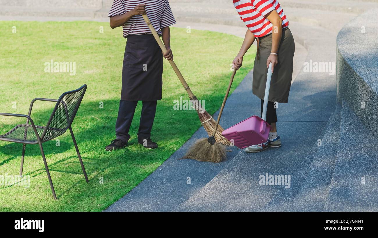 Female worker sweeping yard with broom tool and dustpan in ornamental ...