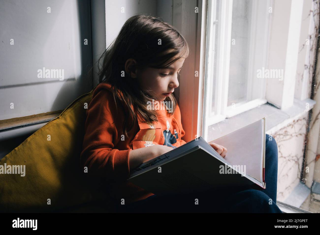 Girl reading book sitting by glass window at home Stock Photo - Alamy