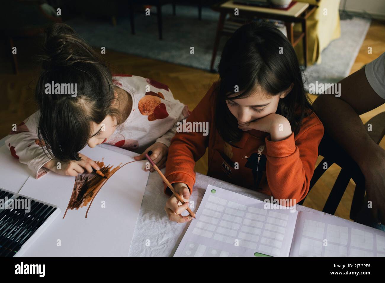 Girl doing homework while sister drawing at table Stock Photo - Alamy
