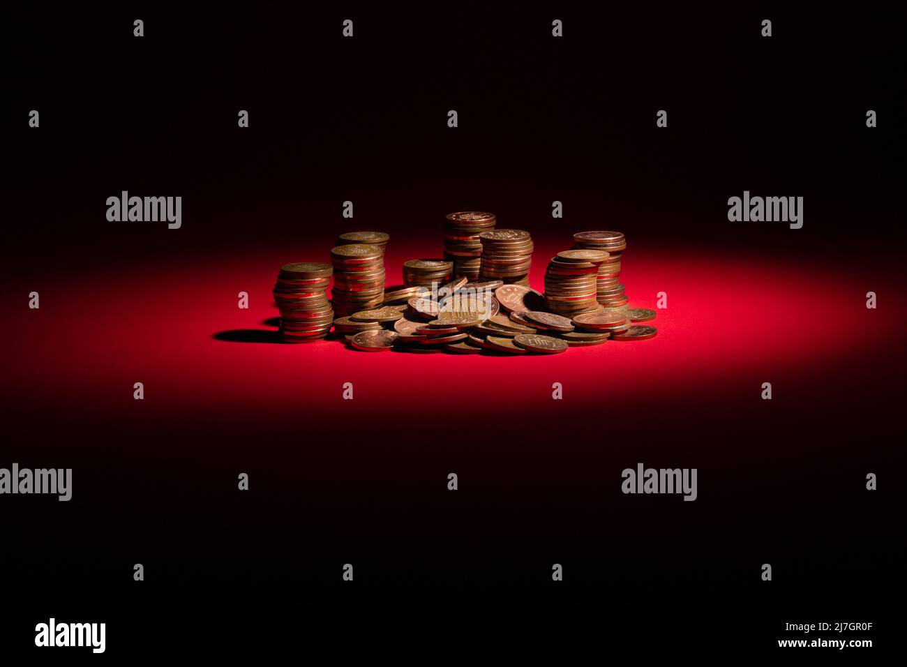 Piles and stacks of UK GBP 1p penny coins spotlit on a red background ...