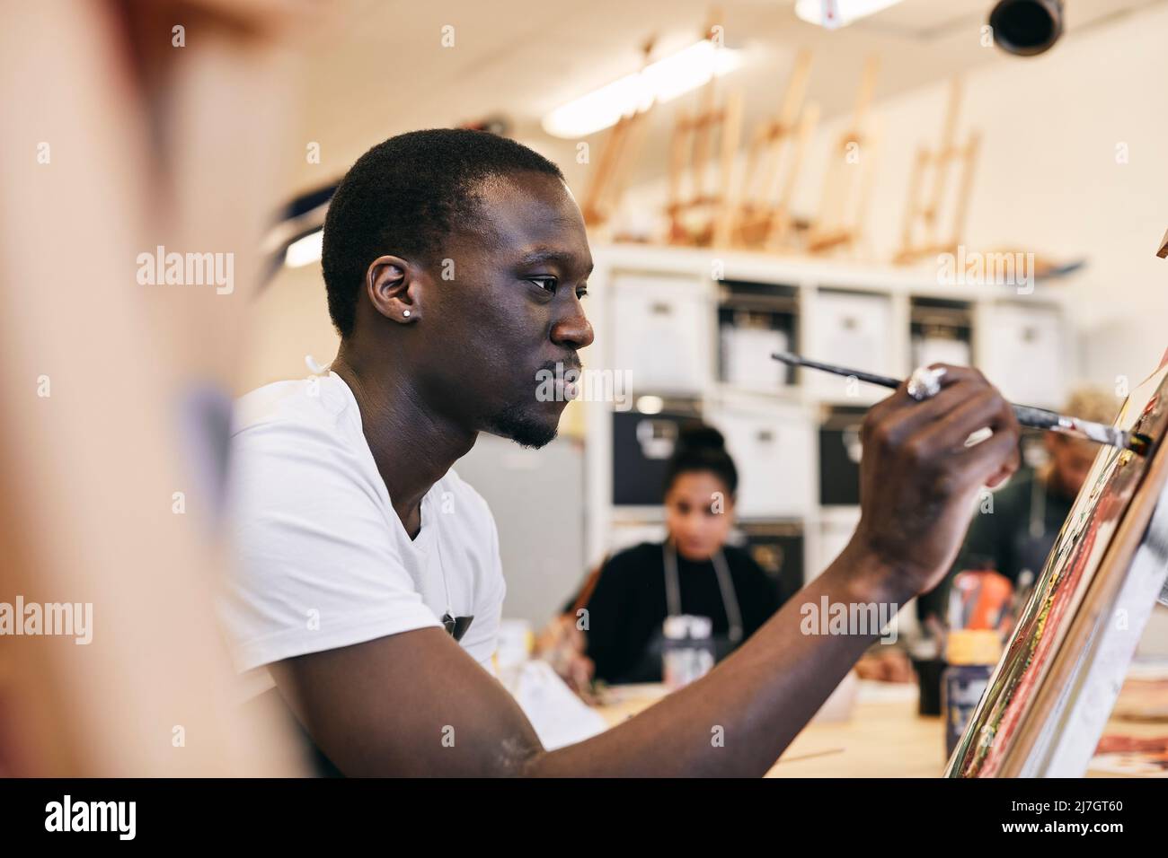 Side view of young male student painting on artist's canvas in art ...