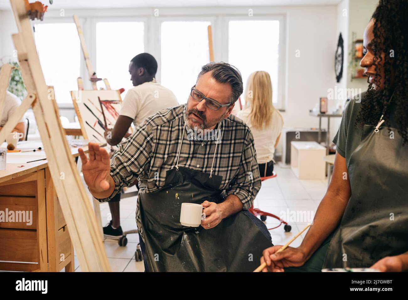 Male instructor explaining female student over artist's canvas in art ...