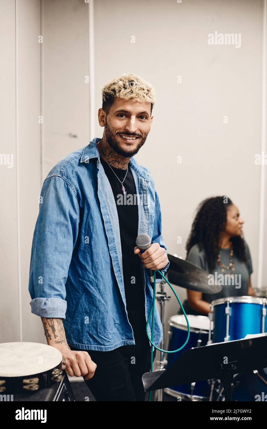 Portrait of smiling young artist holding microphone standing in ...