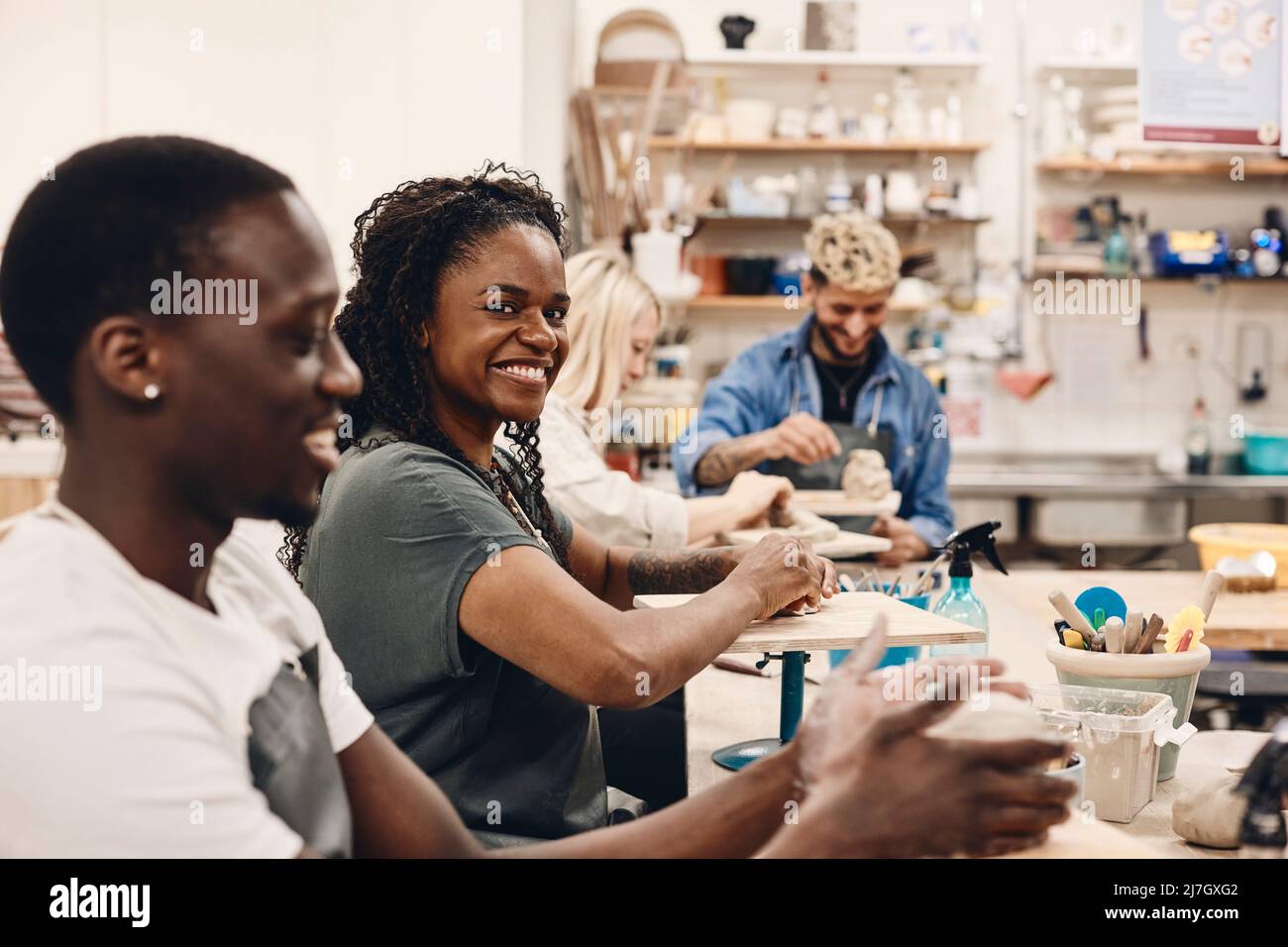 Portrait of smiling woman molding clay sitting by man in art class ...