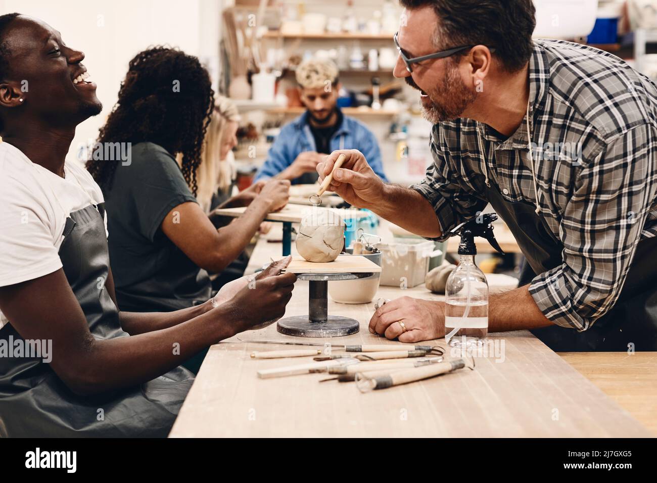 Cheerful mature man with work tool laughing while looking at student in ...