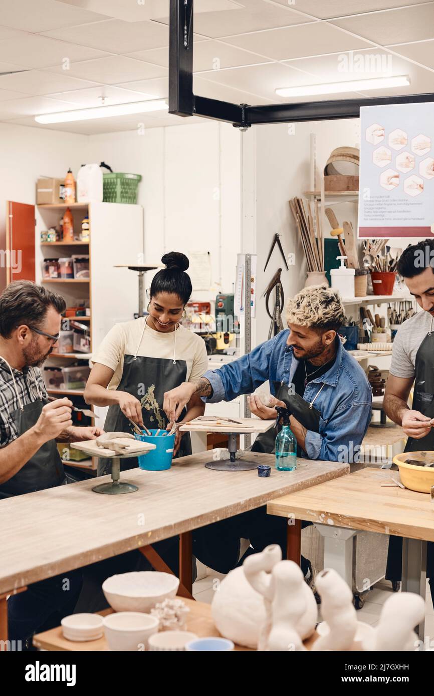 Smiling woman sharing work tools with artists sitting at table in art ...