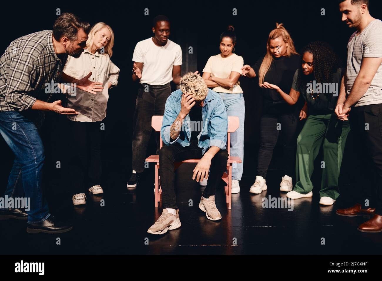 Distraught man scratching head while sitting amidst angry multiracial ...