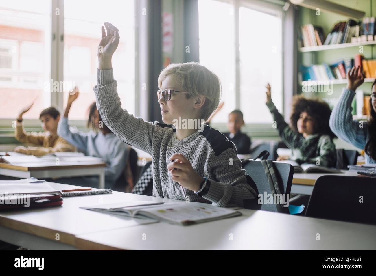 Boy with hand raised attending lecture in classroom Stock Photo - Alamy