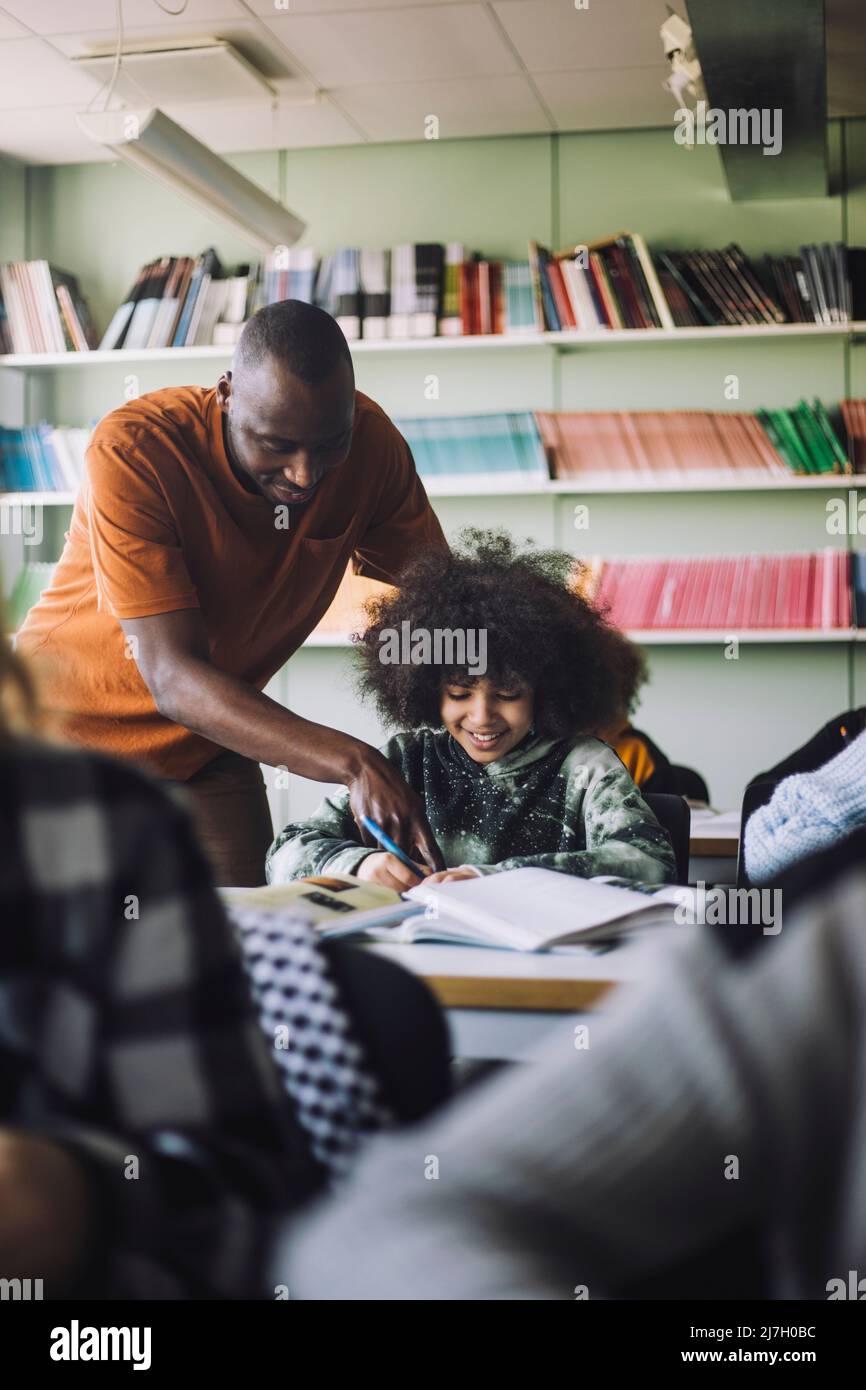 Teacher explaining student while studying in classroom Stock Photo - Alamy