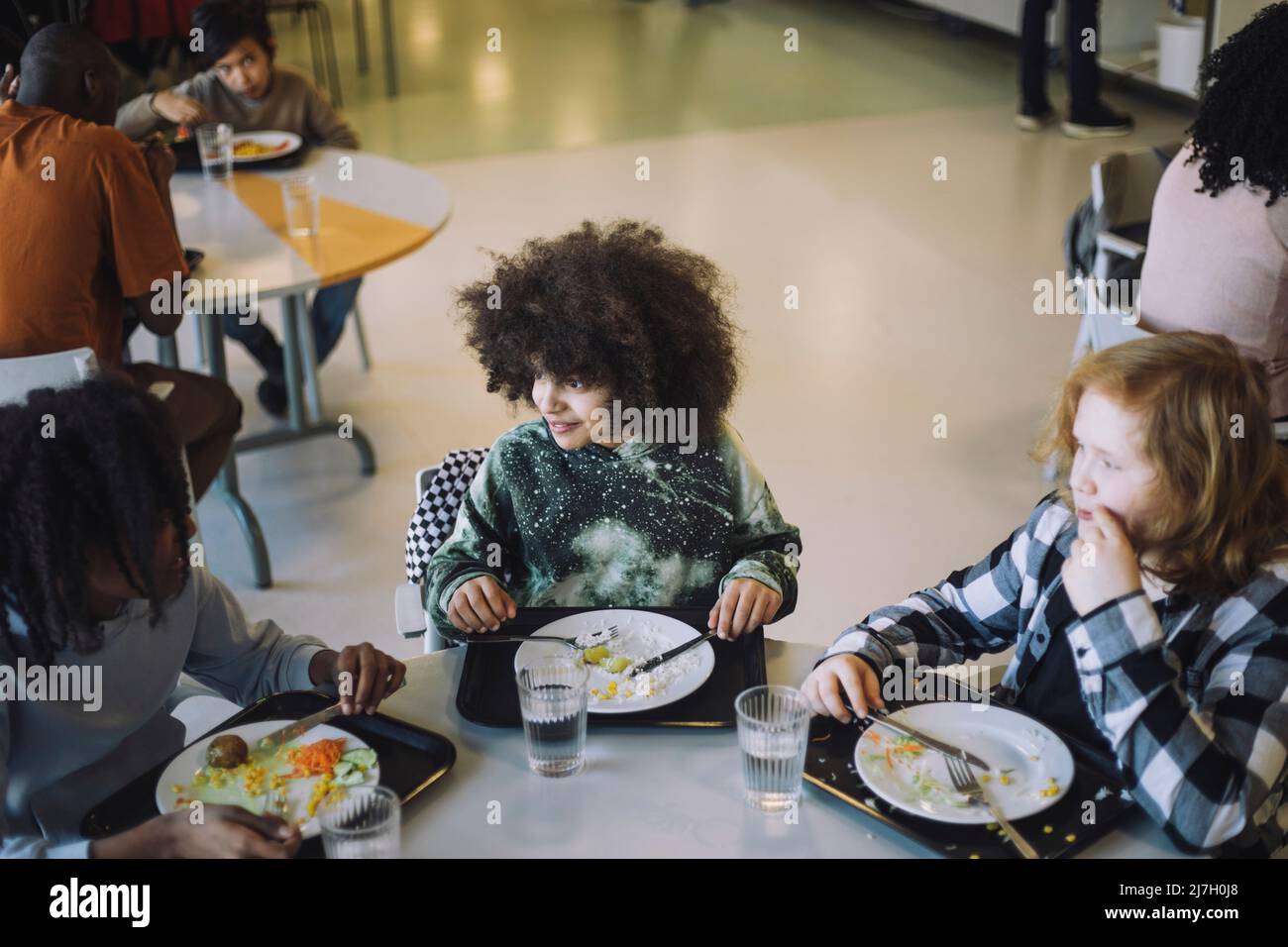 Friends talking to each other sitting at table during lunch break in ...