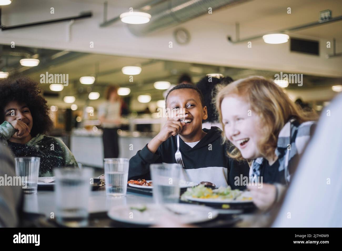 Friends laughing while having food at table during lunch break in ...