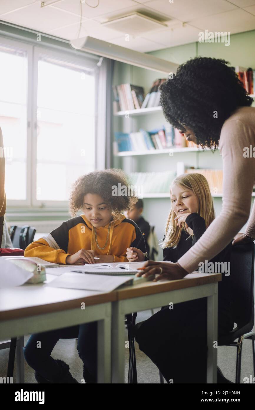 Students looking at book while teacher explaining in classroom Stock ...