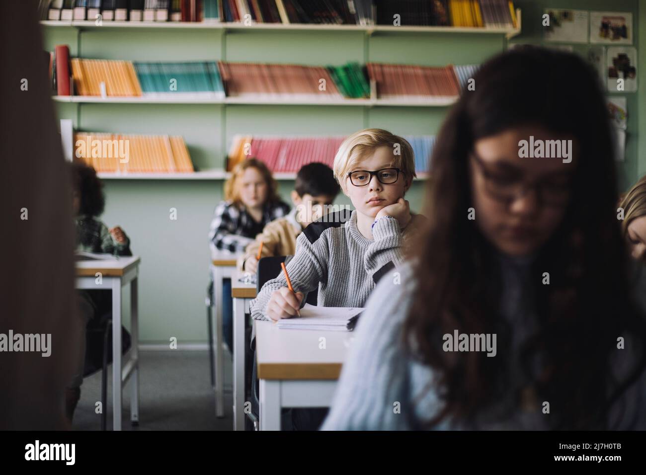 Sad boy with hand on chin sitting at desk in classroom Stock Photo - Alamy