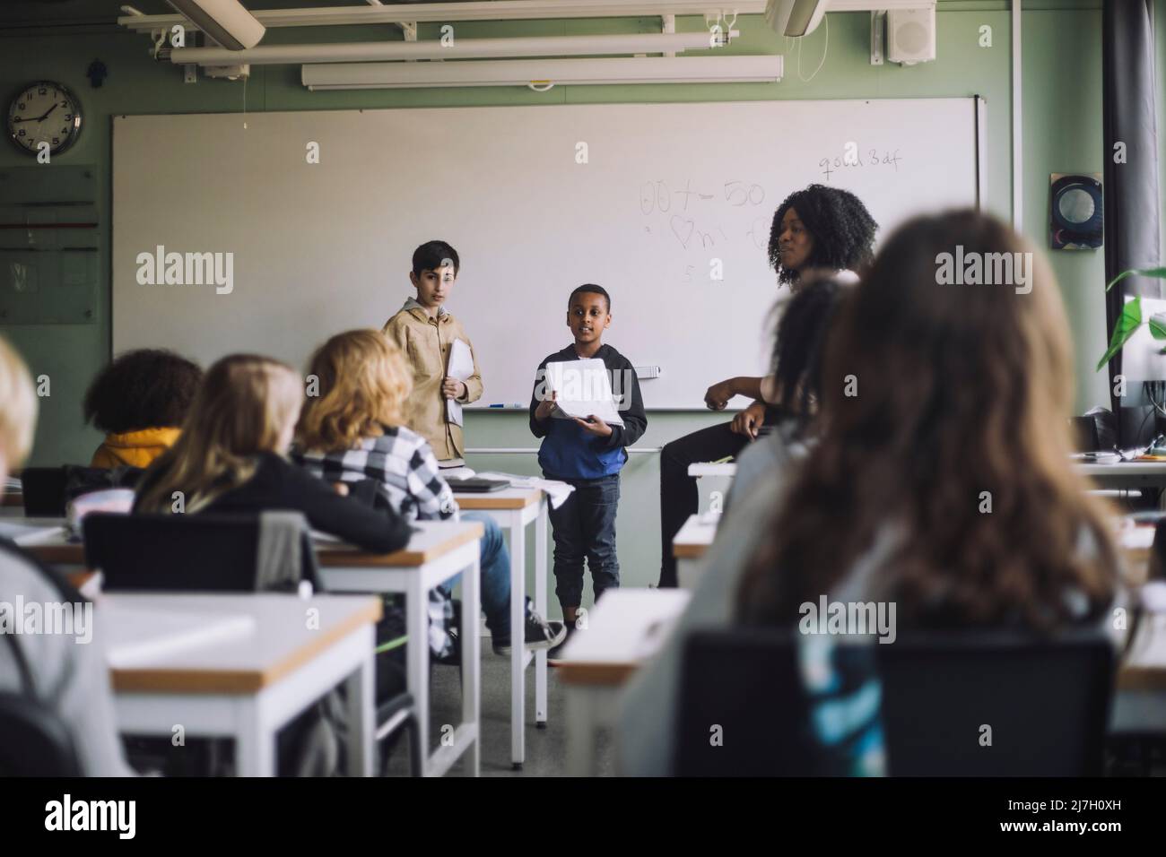 Boys holding reports while doing presentation to students in classroom ...