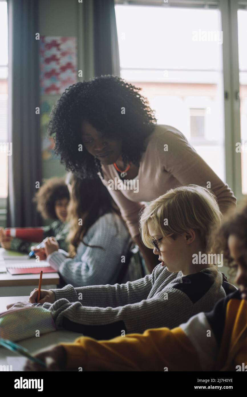 Teacher assisting student while writing in classroom Stock Photo - Alamy
