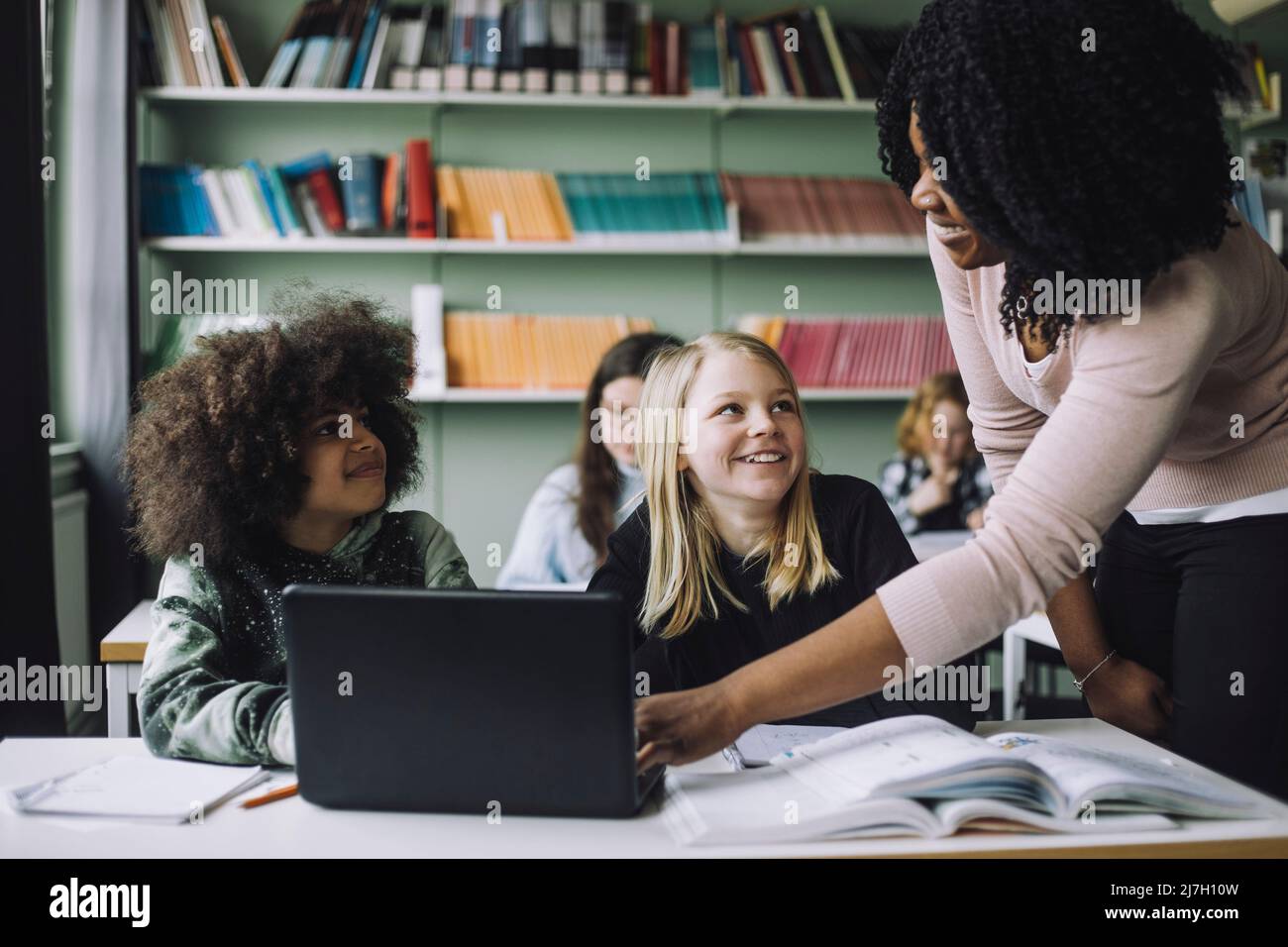 Boy and girl looking at teacher while doing e-learning in classroom ...