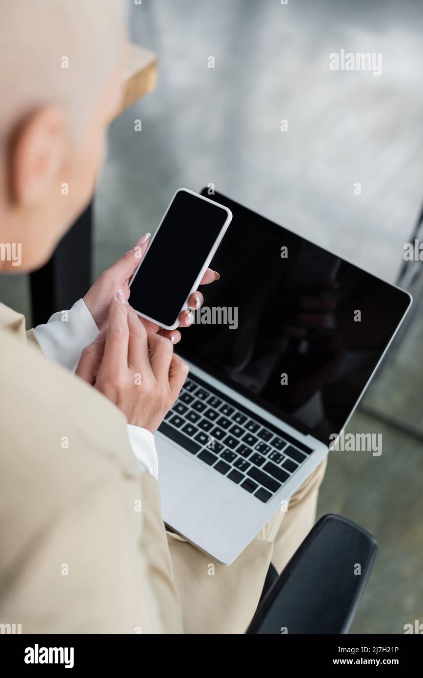 partial view of blurred banker with laptop and smartphone with blank ...