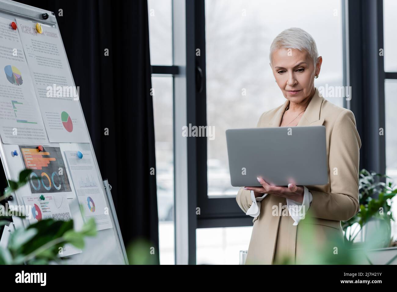 pensive banker with laptop standing near flip chart with analytics in ...
