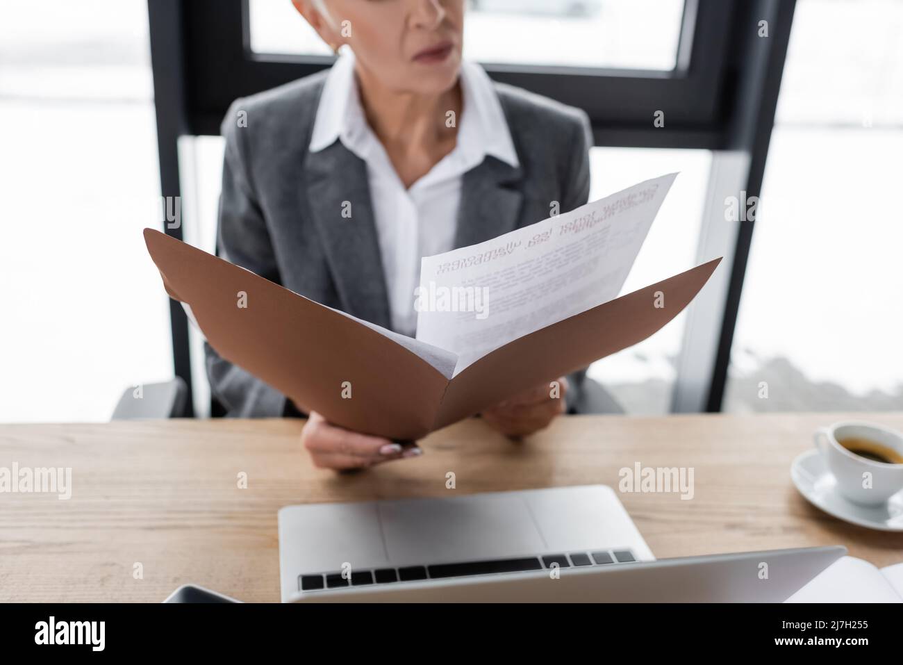 partial view of blurred banker holding folder with documents near ...