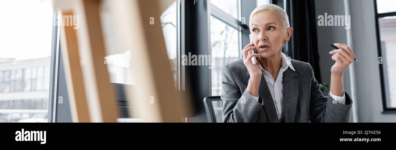 banker holding pen while talking on mobile phone on blurred background ...