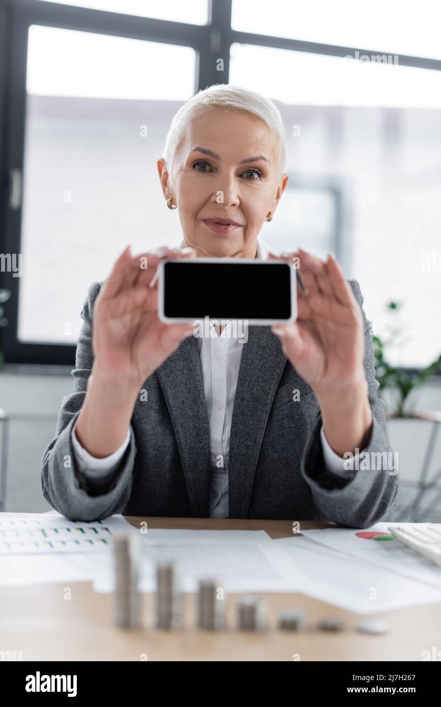 positive banker holding mobile phone with blank screen while looking at ... positive banker holding mobile phone with blank screen while looking at ...