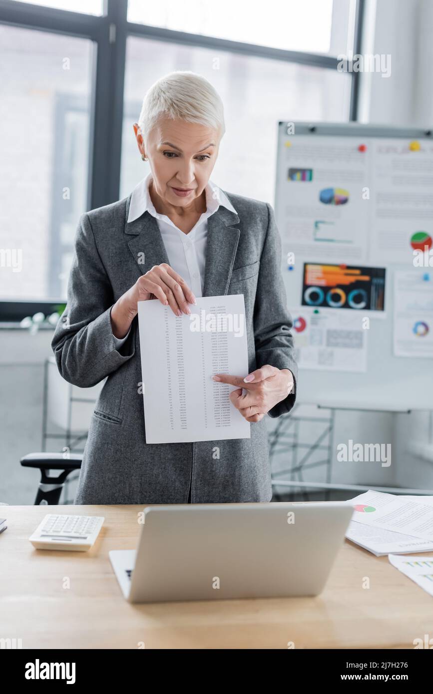 banker pointing at document during video chat on laptop near blurred ...