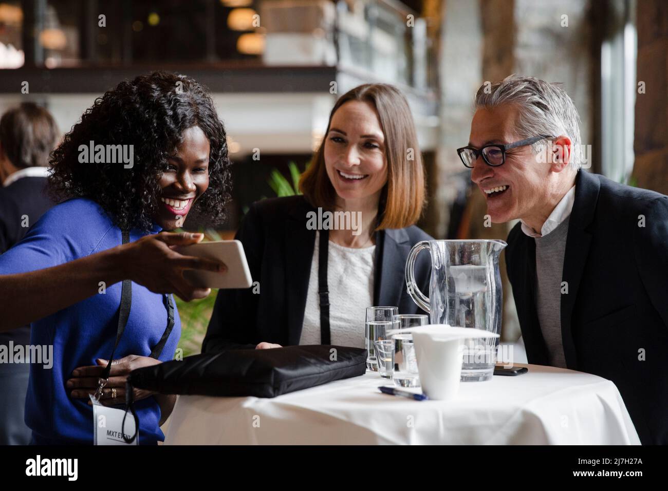 Happy businesswoman sharing smart phone to delegates during meeting in ...