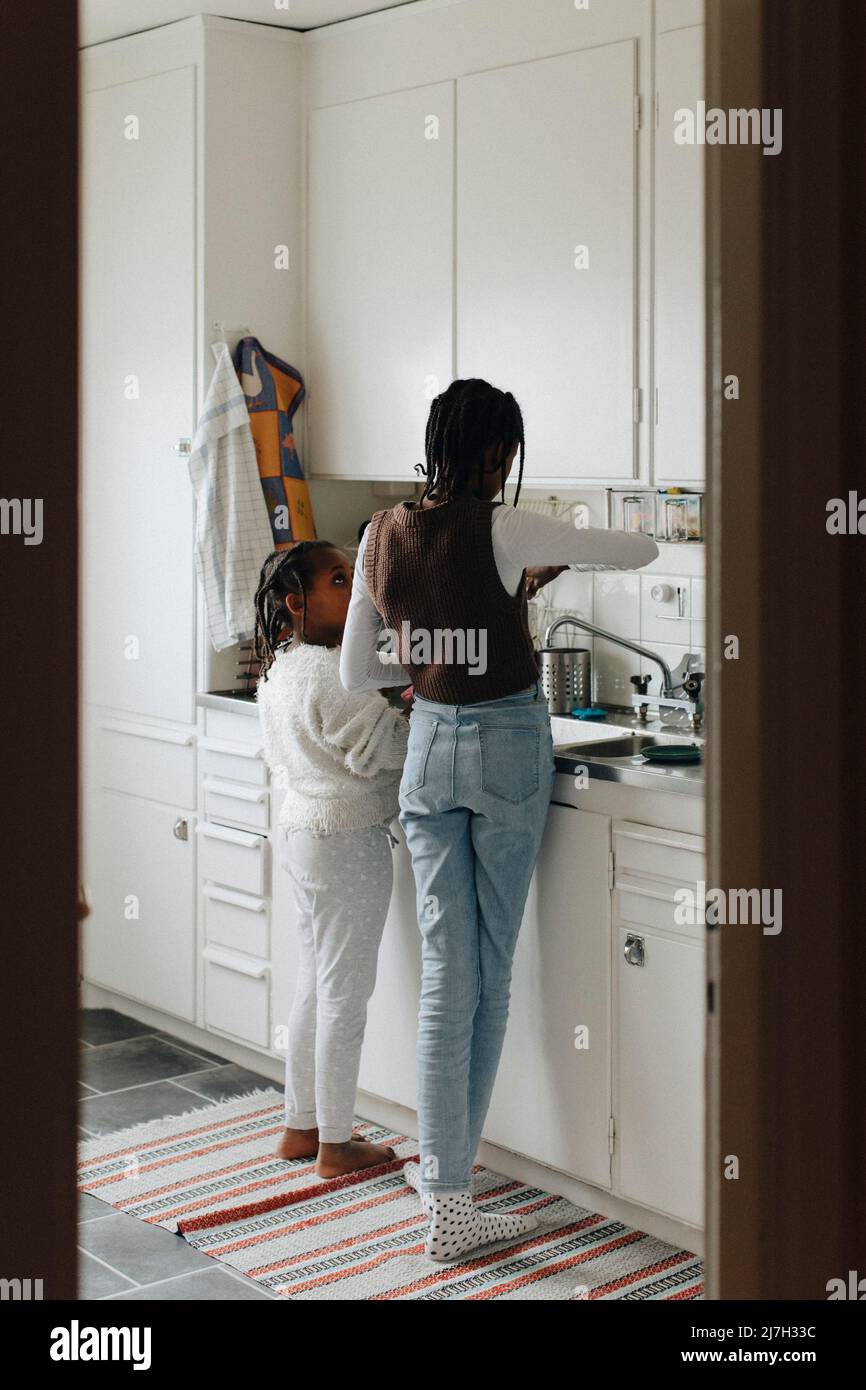 Rear view of sisters standing together in kitchen at home Stock Photo ...