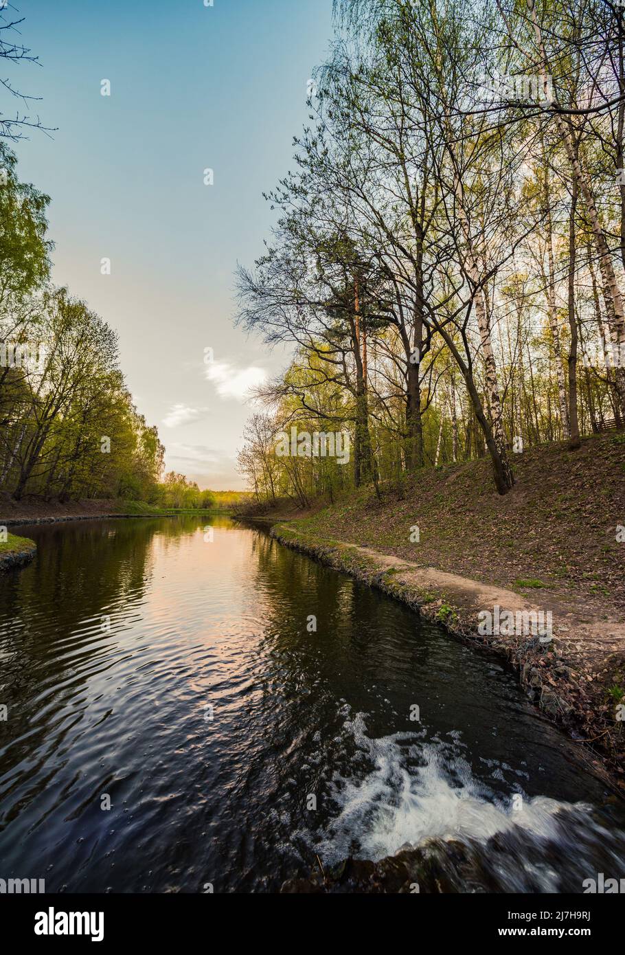 Small river with a reinforced banks in forest park, springtime evening ...