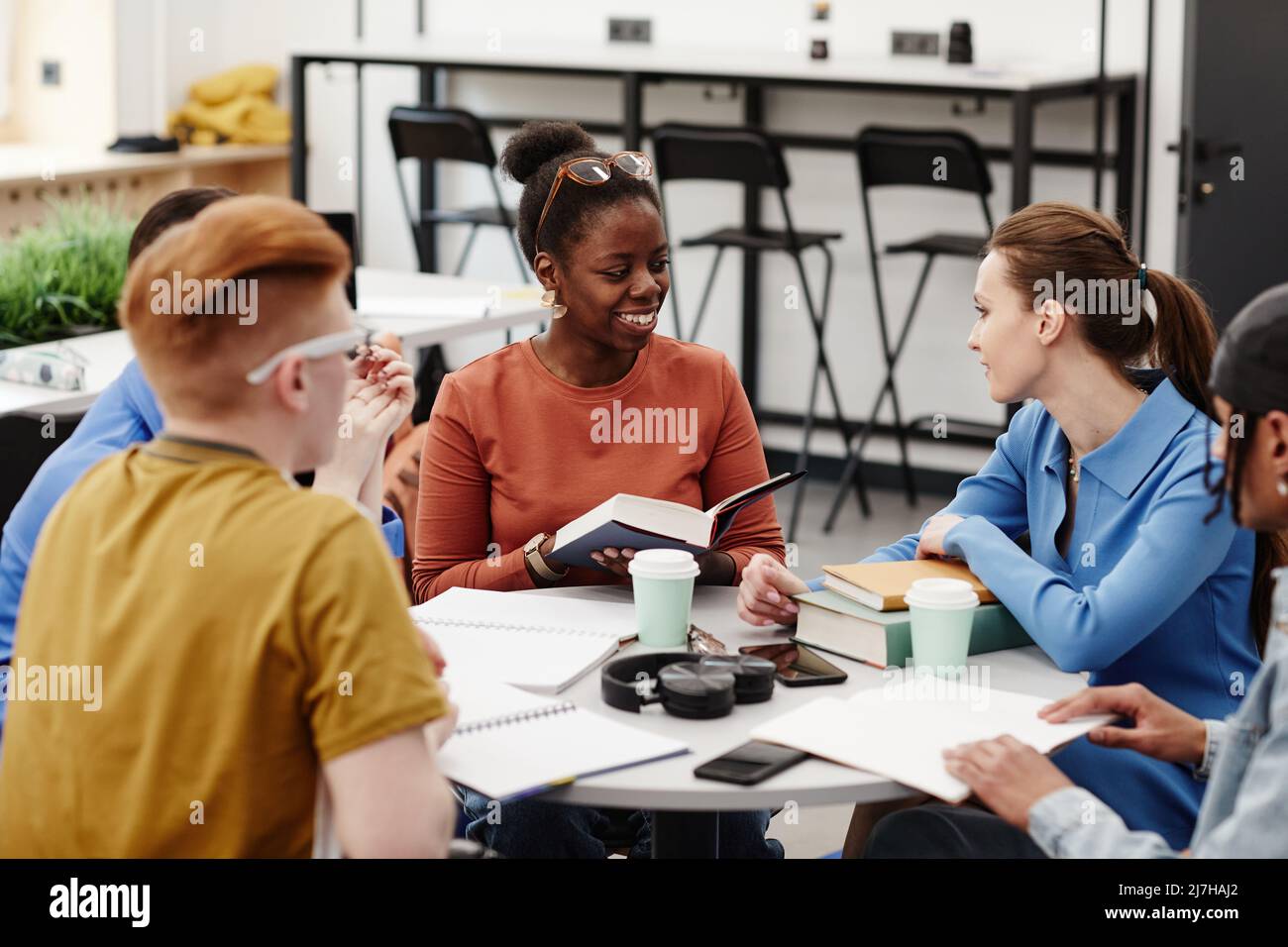 Cheerful group of young people studying together at round table in ...