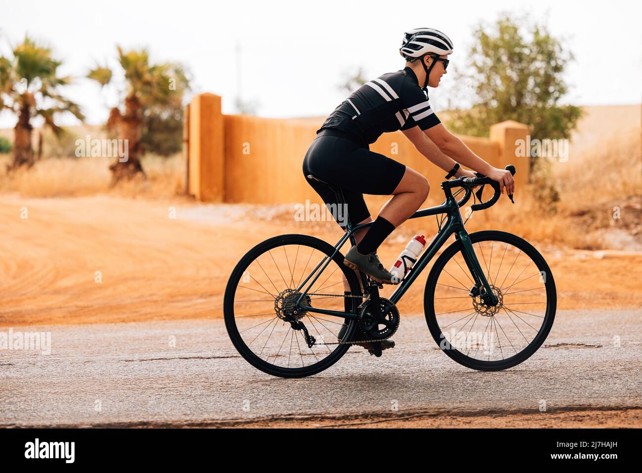 Side view of female cyclist riding bicycle on countryside road ...