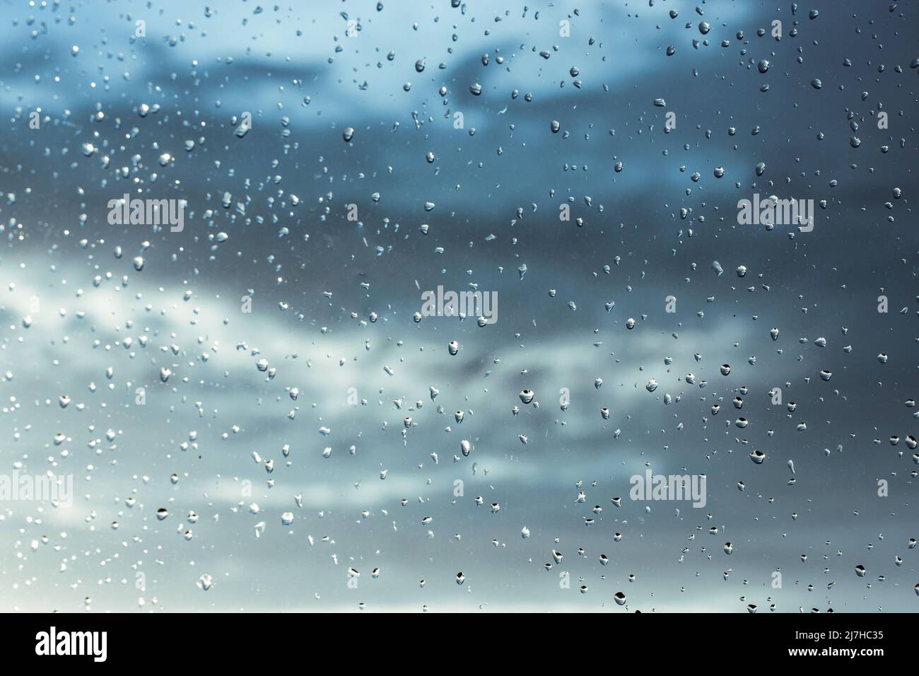 Window with small raindrops on the surface of a glass against a blue ...