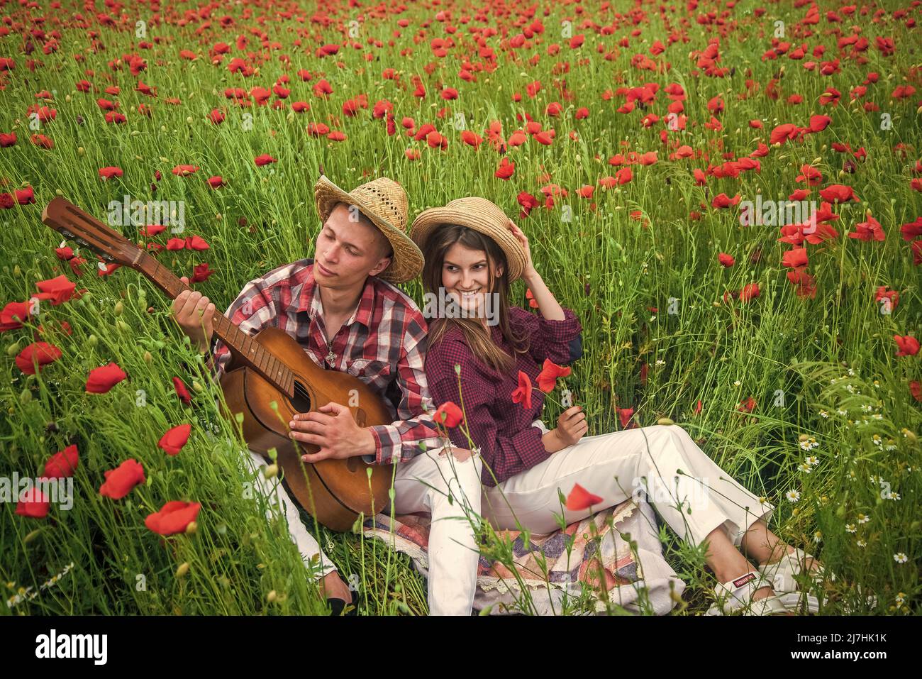 romantic couple playing guitar music in a field with red flowers ...