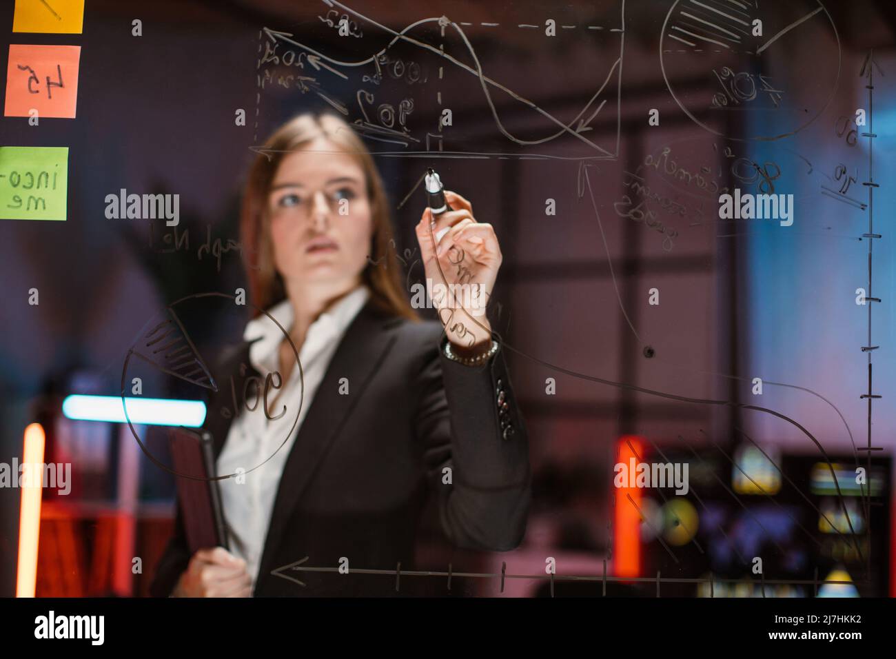 Blur view of pretty Caucasian woman in formal wear writing charts on ...